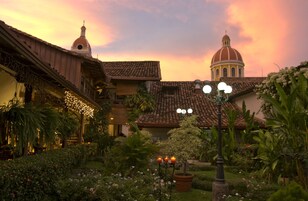 Um pátio com jardim, um edifício com cúpula e um campanário.