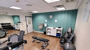 Uma academia com equipamentos de exercícios, uma mesa de recepção e um relógio fixado na parede.