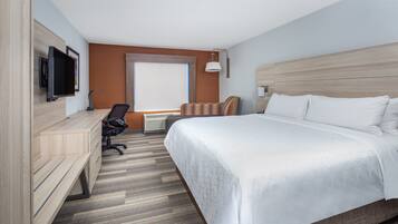 Quarto de hotel com cama, escrivaninha, cadeira, televisão e janela.
