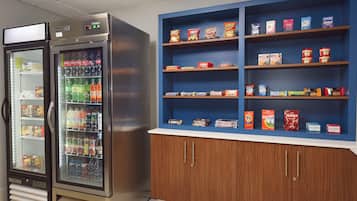 Máquina de vendas com diversas bebidas e lanches, e uma estante com alimentos embalados.