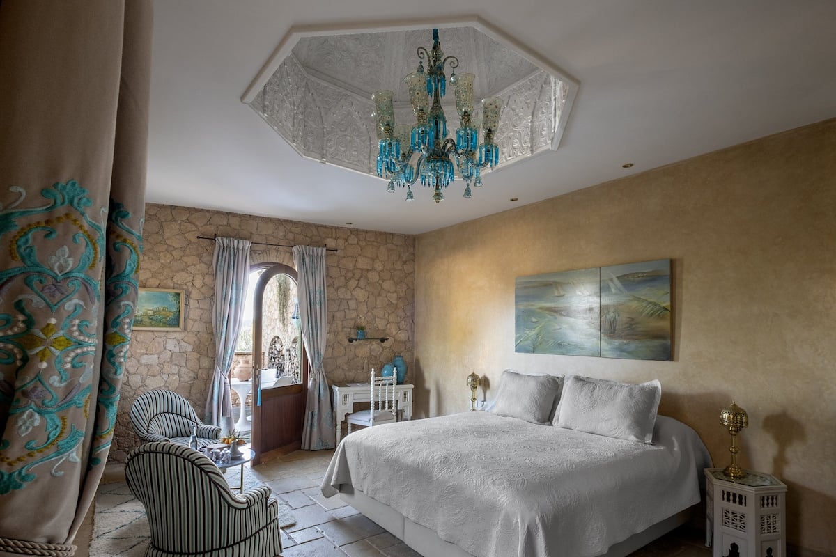 Quarto com uma cama grande, um candelabro, uma pintura e uma parede de pedra.