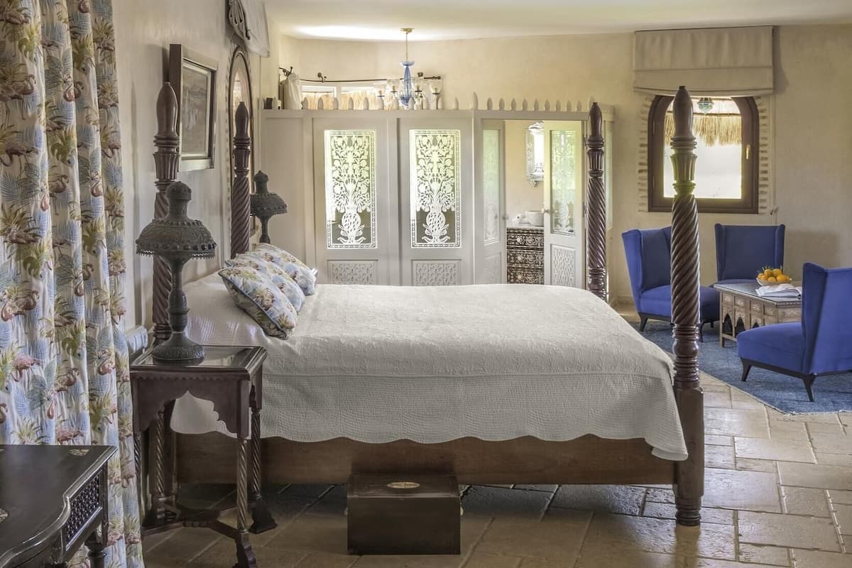 Quarto com uma cama grande, um candelabro, uma cadeira de madeira e uma mesa.