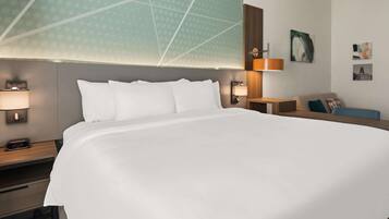 Quarto de hotel com uma cama grande, duas mesas de cabeceira com luminárias, um painel de cabeceira em madeira e obras de arte nas paredes.