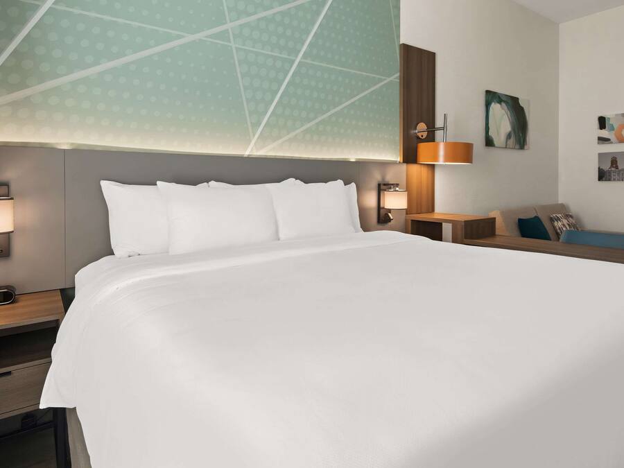 Quarto de hotel com uma cama grande, duas mesas de cabeceira com luminárias, um painel de cabeceira em madeira e obras de arte nas paredes.