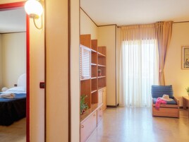 Quarto com cama, guarda-roupa de madeira, janela com cortinas e uma pequena mesa com chapéu e cachecol.