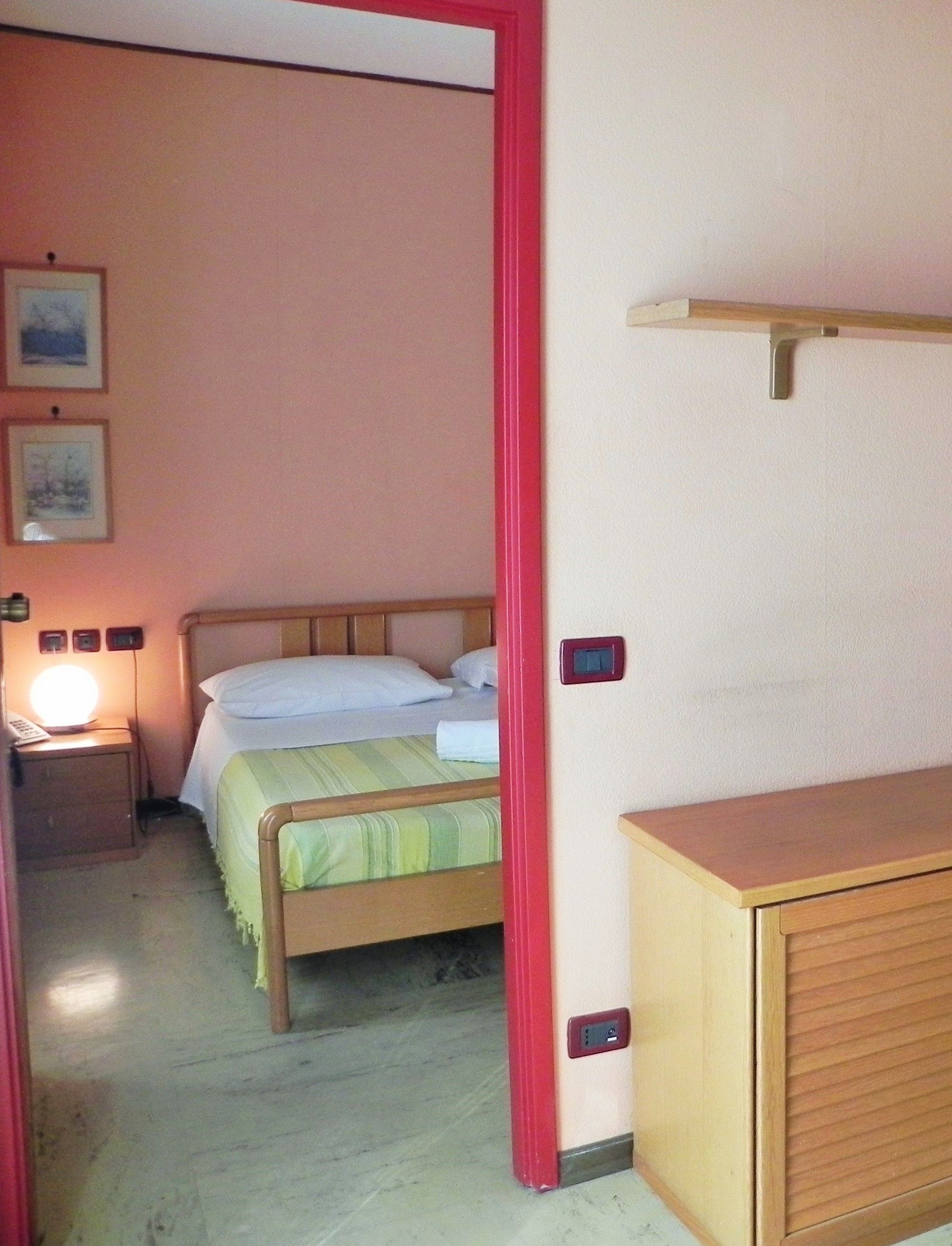 Quarto pequeno com uma cama de solteiro, cabeceira de madeira, mesa de cabeceira com luminária e um armário de madeira.