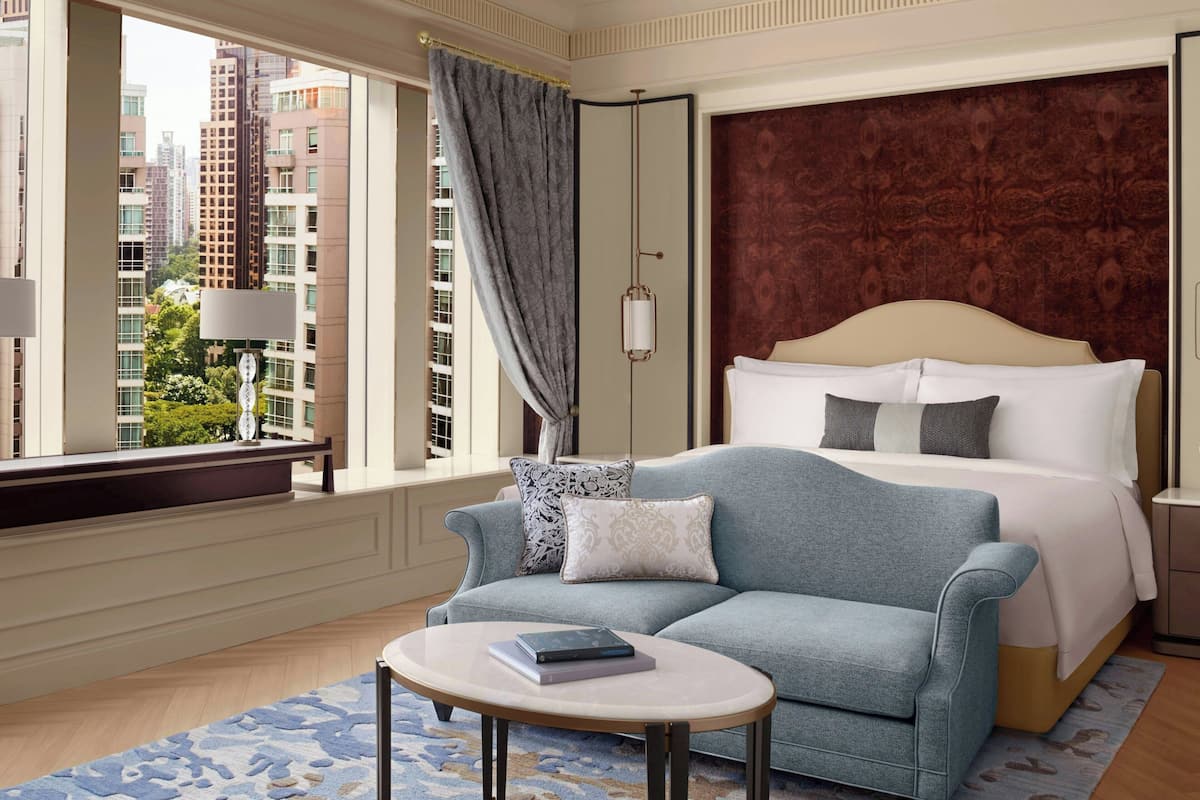 Quarto de hotel com uma cama grande, um sofá, uma mesa pequena e vista para edifícios altos.