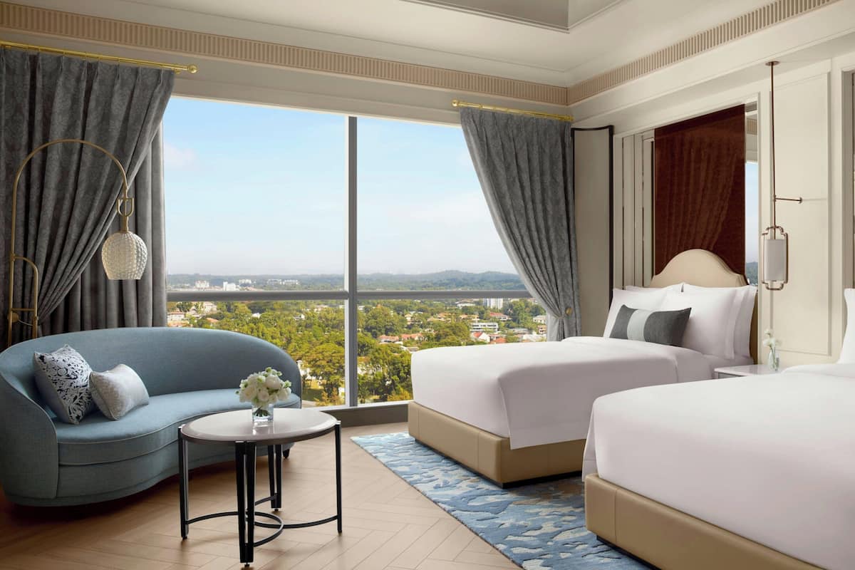 Quarto de hotel com duas camas, um sofá, uma mesinha e vista para a paisagem urbana.