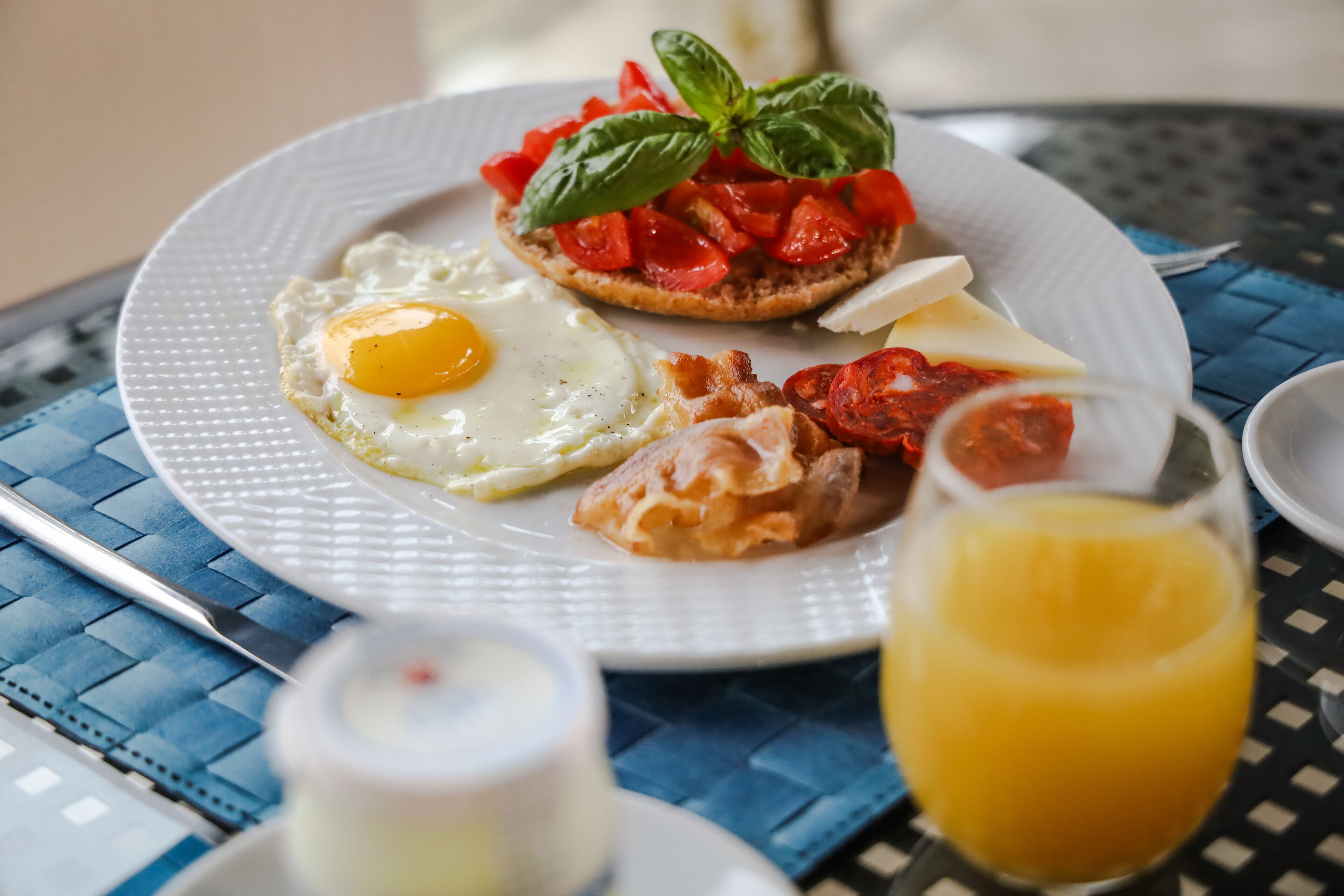 Prato de café da manhã com ovos, bacon, tomates e queijo sobre um tapete de mesa trançado.