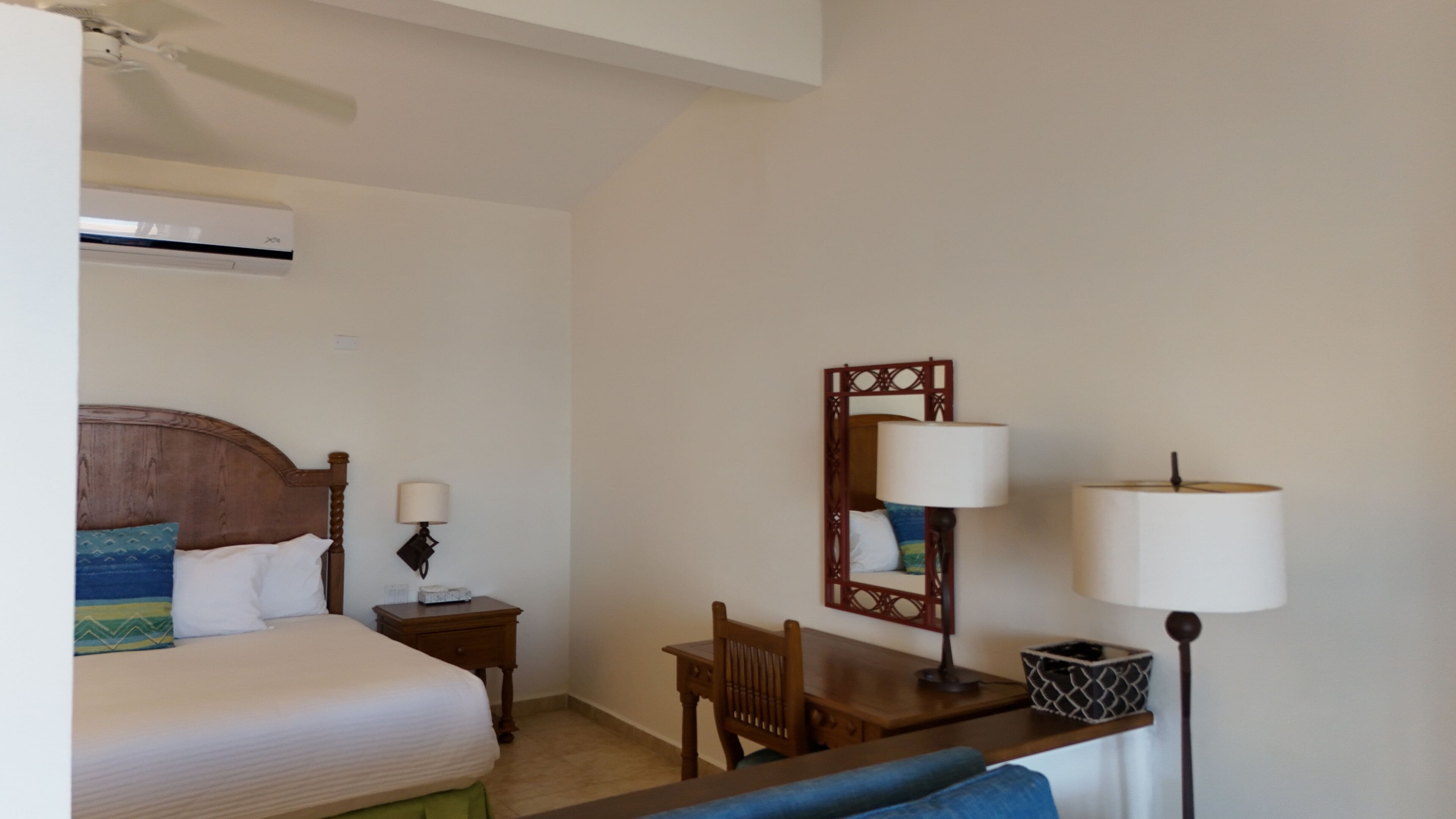 Quarto de hotel com cama, escrivaninha, cadeira, espelho e luminária.