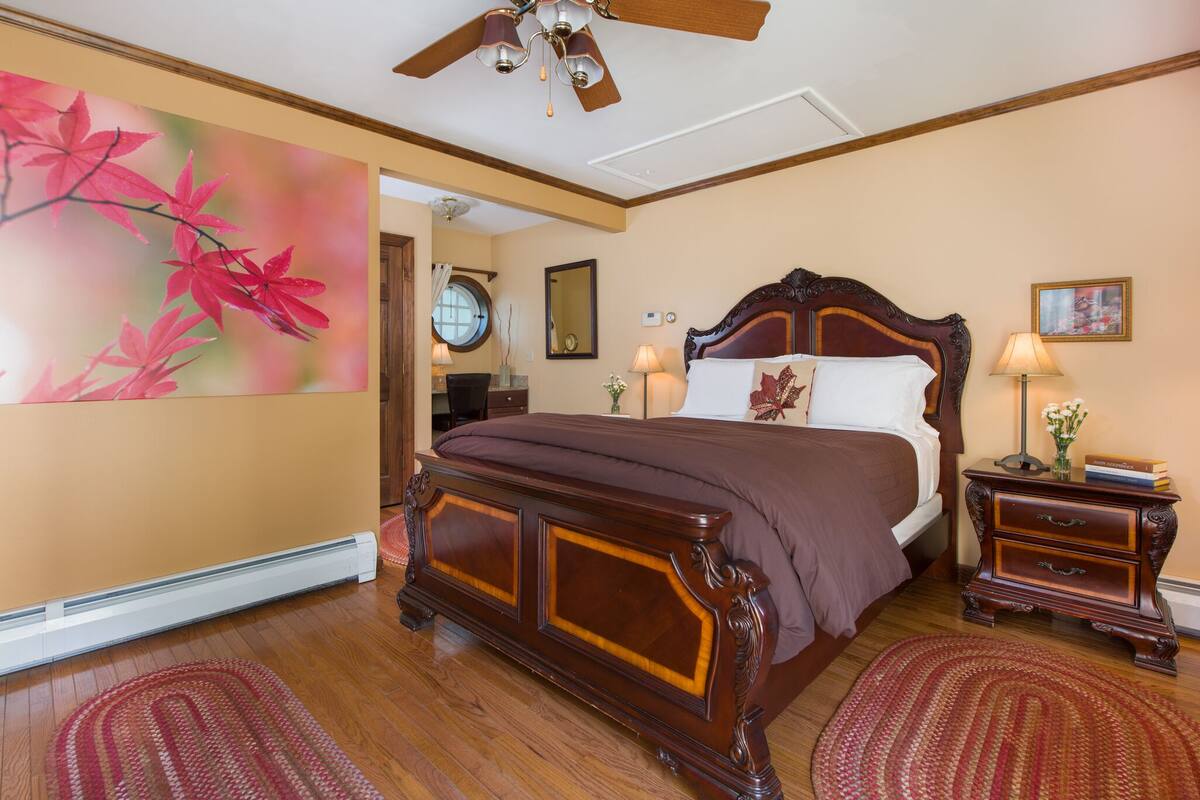 Quarto com uma cama grande, um ventilador de teto, mesa de cabeceira com abajur e um quadro na parede.