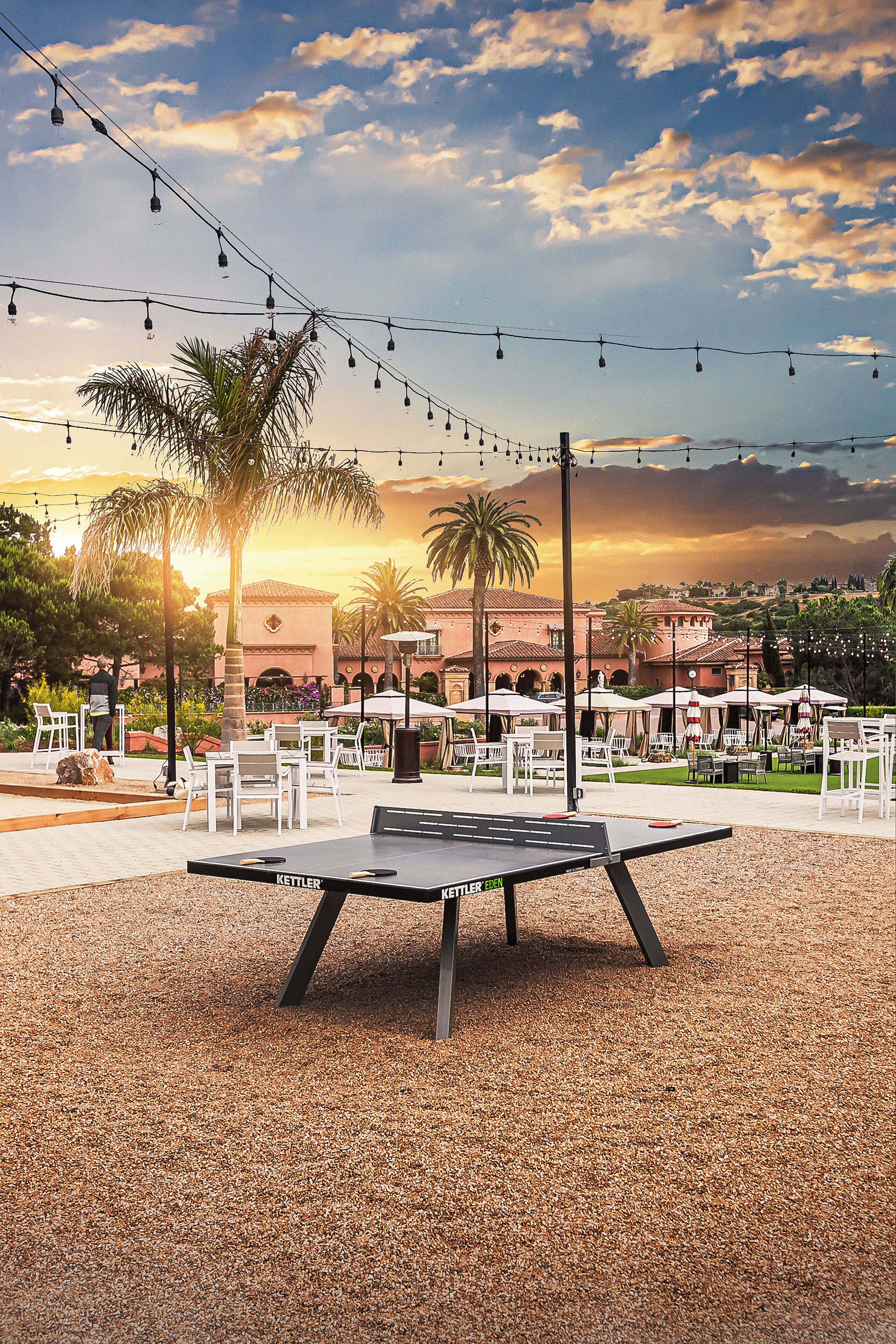 Área externa com mesas, cadeiras, mesa de pingue-pongue e luzes de Natal ao pôr do sol.