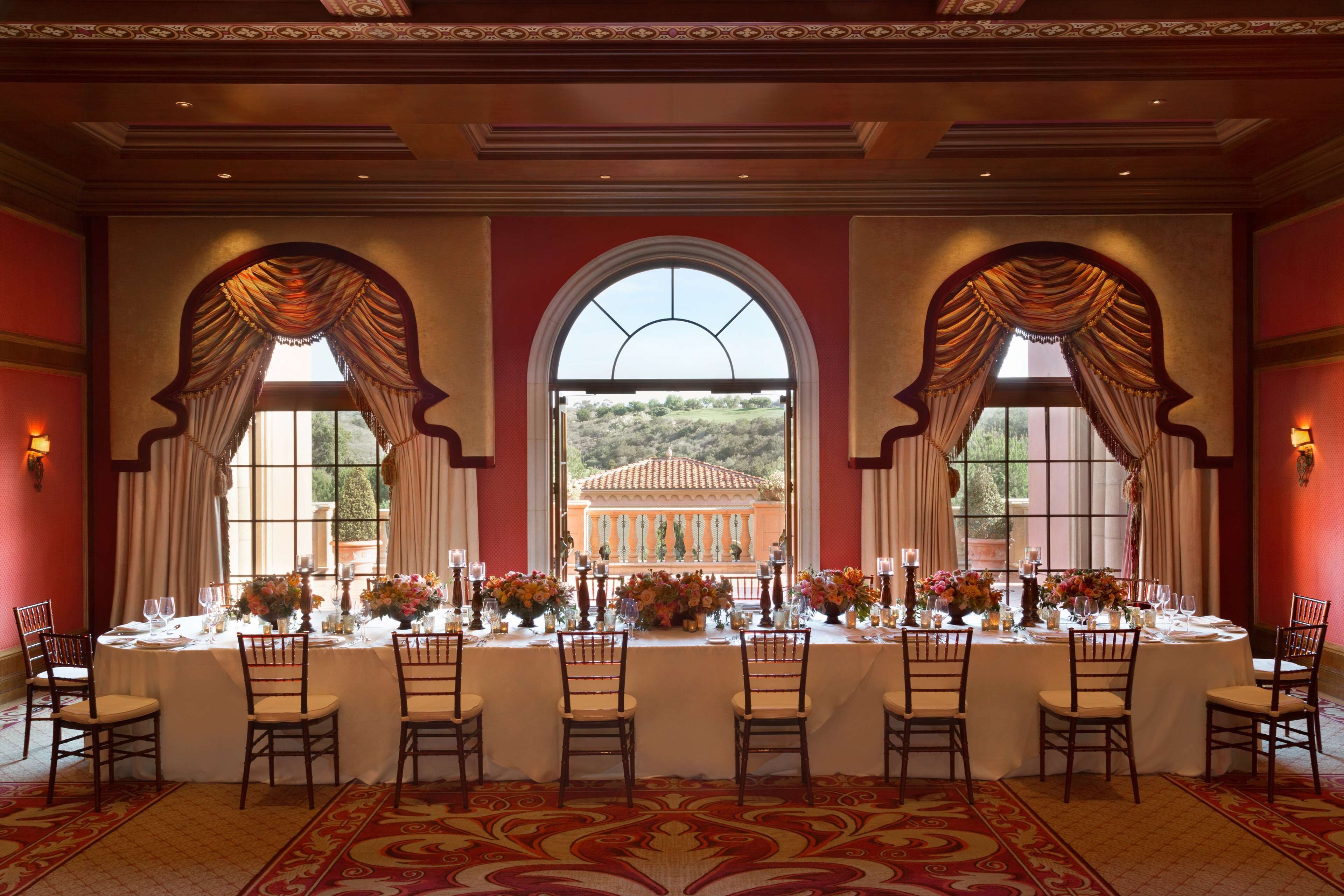 Uma sala de jantar formal com uma mesa posta para seis pessoas, amplas janelas em arco e vista de um edifício ao fundo.