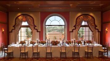 Uma sala de jantar formal com uma mesa posta para seis pessoas, amplas janelas em arco e vista de um edifício ao fundo.