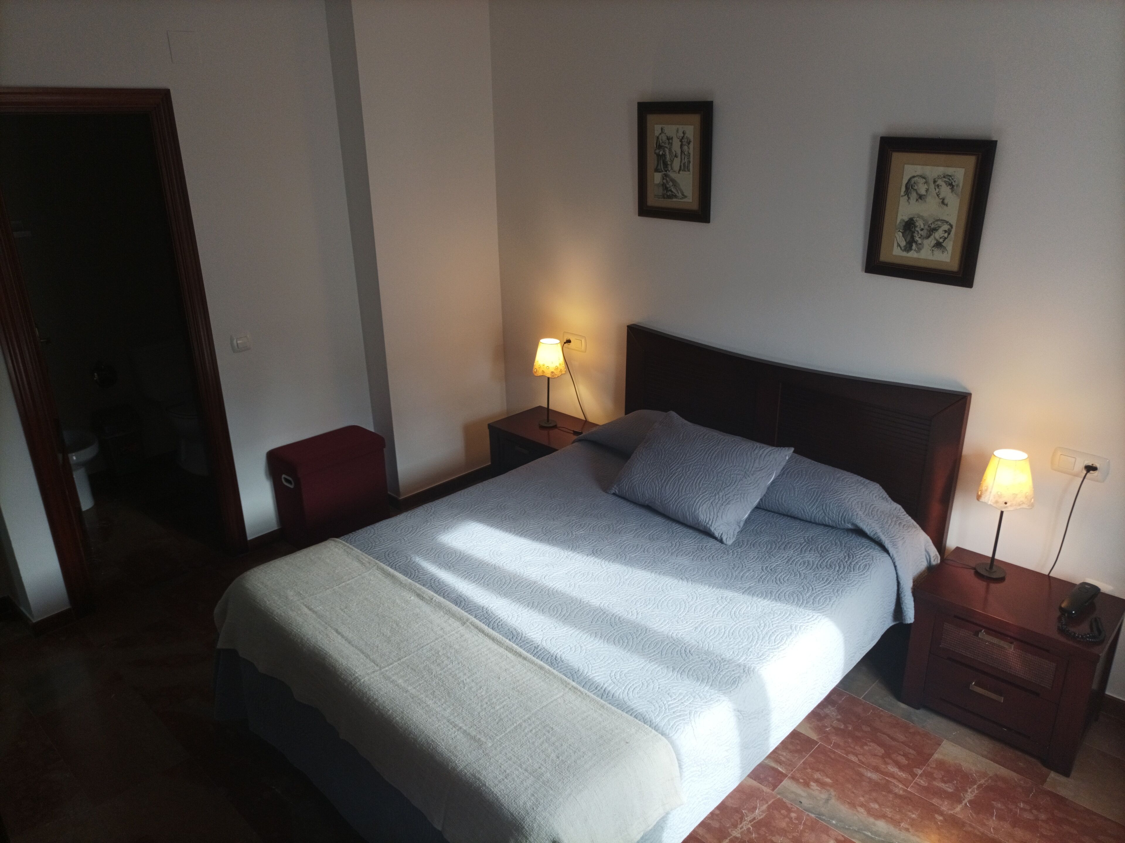 Quarto com uma cama, duas mesas de cabeceira, duas luminárias de parede e duas imagens emolduradas.