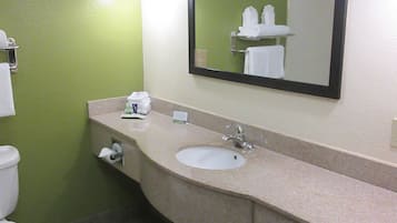 Casa de banho com parede verde, sanita branca, lavatório com espelho em cima e um porta-toalhas com toalhas.