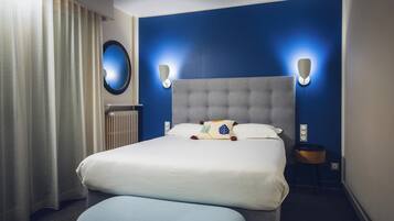 Quarto de hotel com uma cama grande, duas luzes fixadas na parede, um espelho redondo e um radiador.