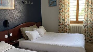 Quarto de hotel com duas camas, cabeceira, pintura, telefone e janela com cortinas.