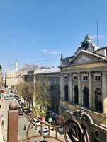 Um edifício histórico com arquitetura clássica, incluindo uma estátua imponente no telhado e uma torre do relógio ao fundo.