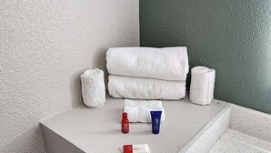 Casa de banho com lavatório branco, parede verde e bancada com produtos de higiene pessoal, incluindo uma garrafa vermelha, um tubo azul e um tubo branco.