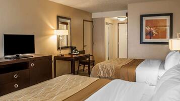 Quarto de hotel com duas camas, uma mesa com abajur, televisão e um quadro na parede.