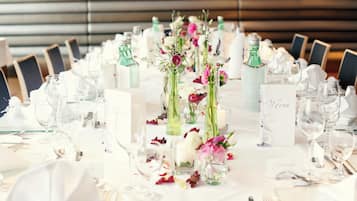 Uma longa mesa de jantar posta para um evento formal, com diversos lugares, cada um com cartão de menu, copos e arranjos florais.