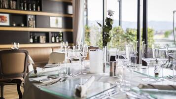 Uma mesa de restaurante posta, com taças de vinho, talheres e um vaso com uma única rosa.