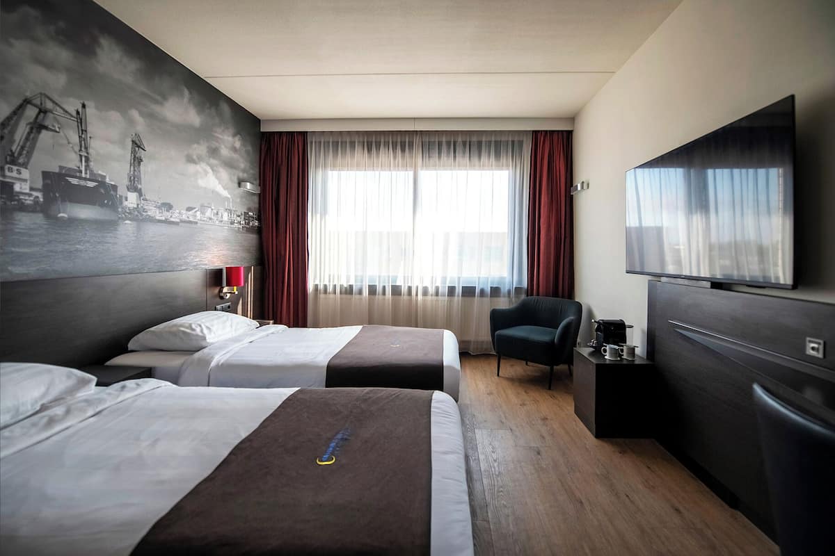 Quarto de hotel com duas camas, televisão, secretária com cafeteira e uma cadeira.