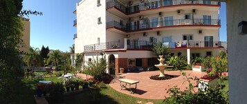 Um edifício residencial com vários andares, varandas, um pátio com uma fonte e área de estar ao ar livre.