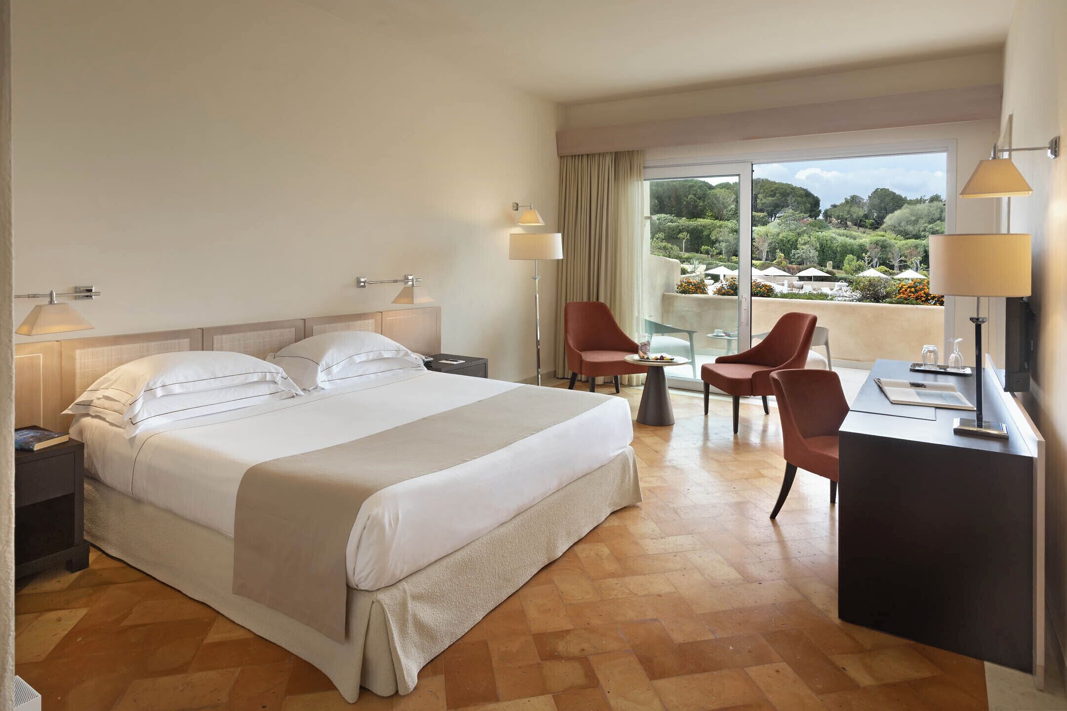 Quarto de hotel com uma cama grande, uma escrivaninha com cadeira e uma varanda com vista.