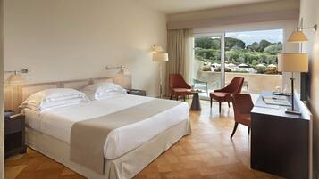 Quarto de hotel com uma cama grande, uma escrivaninha com cadeira e uma varanda com vista.