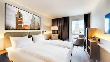 Quarto de hotel com cama grande, escrivaninha, cadeira, luminária, televisão e vista para a cidade.