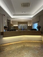 Uma área de recepção moderna com balcão curvo, janela ampla e teto com iluminação embutida.