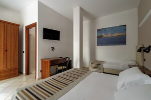 Quarto de hotel com cama, escrivaninha, cadeira, televisão e pintura de paisagem urbana.