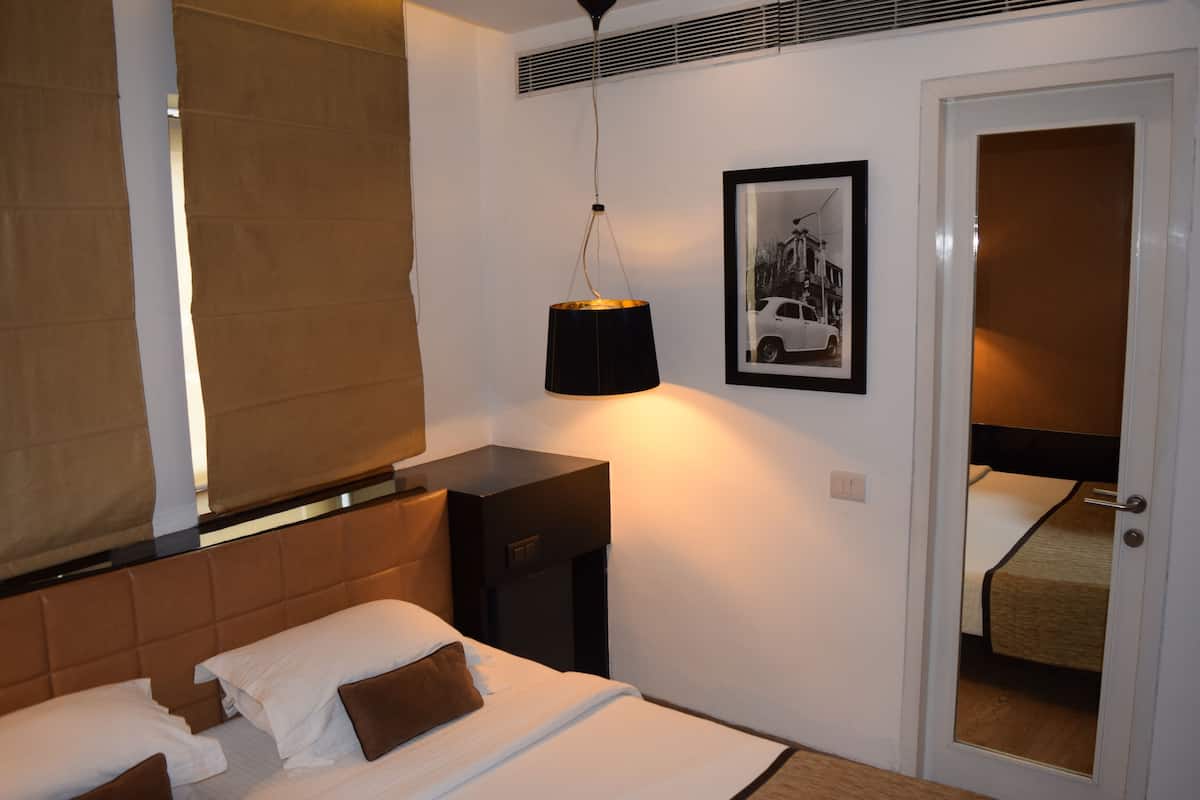 Quarto de hotel com uma cama, mesa de cabeceira, quadro na parede e porta que dá para outro aposento.