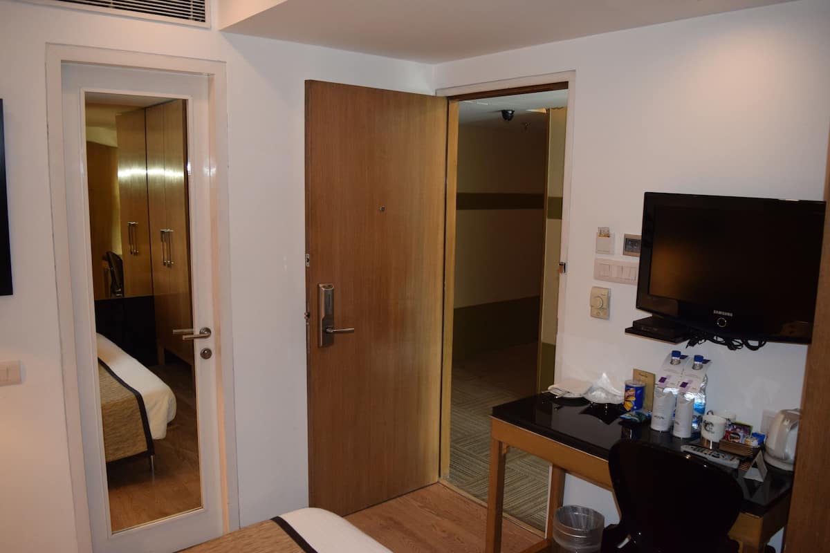 Quarto de hotel com cama, escrivaninha com televisão e porta que dá para outro cômodo.