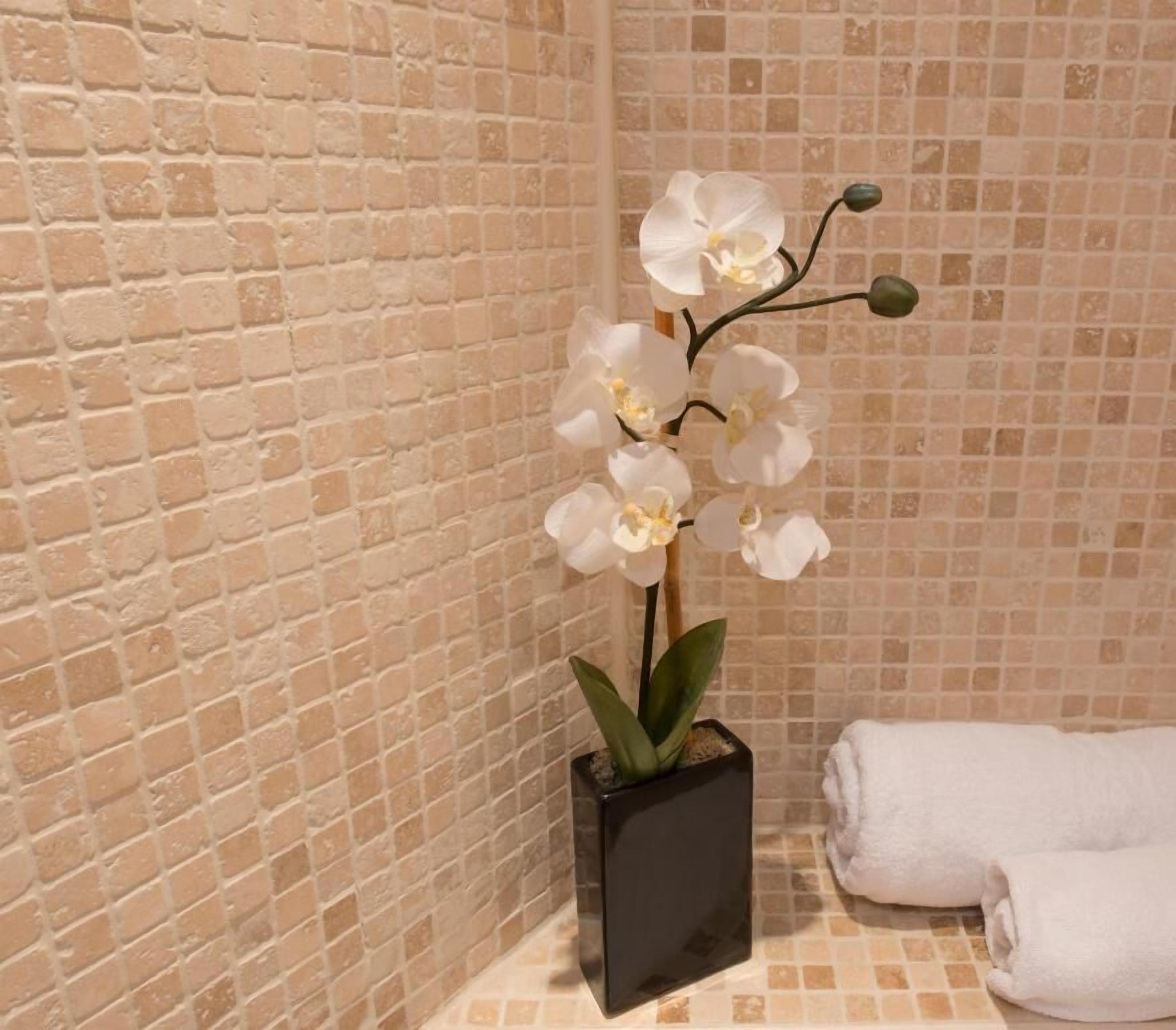 Um banheiro com parede azulejada, uma orquídea em vaso e uma toalha enrolada.