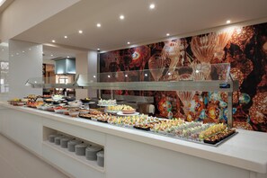 Buffet com diversos alimentos e uma parede decorativa ao fundo.