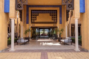 Entrada de hotel com galeria coberta, colunas e área de estar ao ar livre.