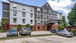 Um hotel Comfort Inn com design moderno, apresentando fachada de tijolos, diversas janelas e um estacionamento com vários carros.