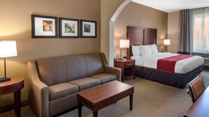 Quarto de hotel com cama, sofá, mesa de centro e quadros na parede.