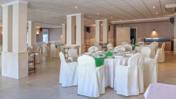 Uma sala de banquetes com mesas redondas, cadeiras brancas e um caminho de mesa verde.