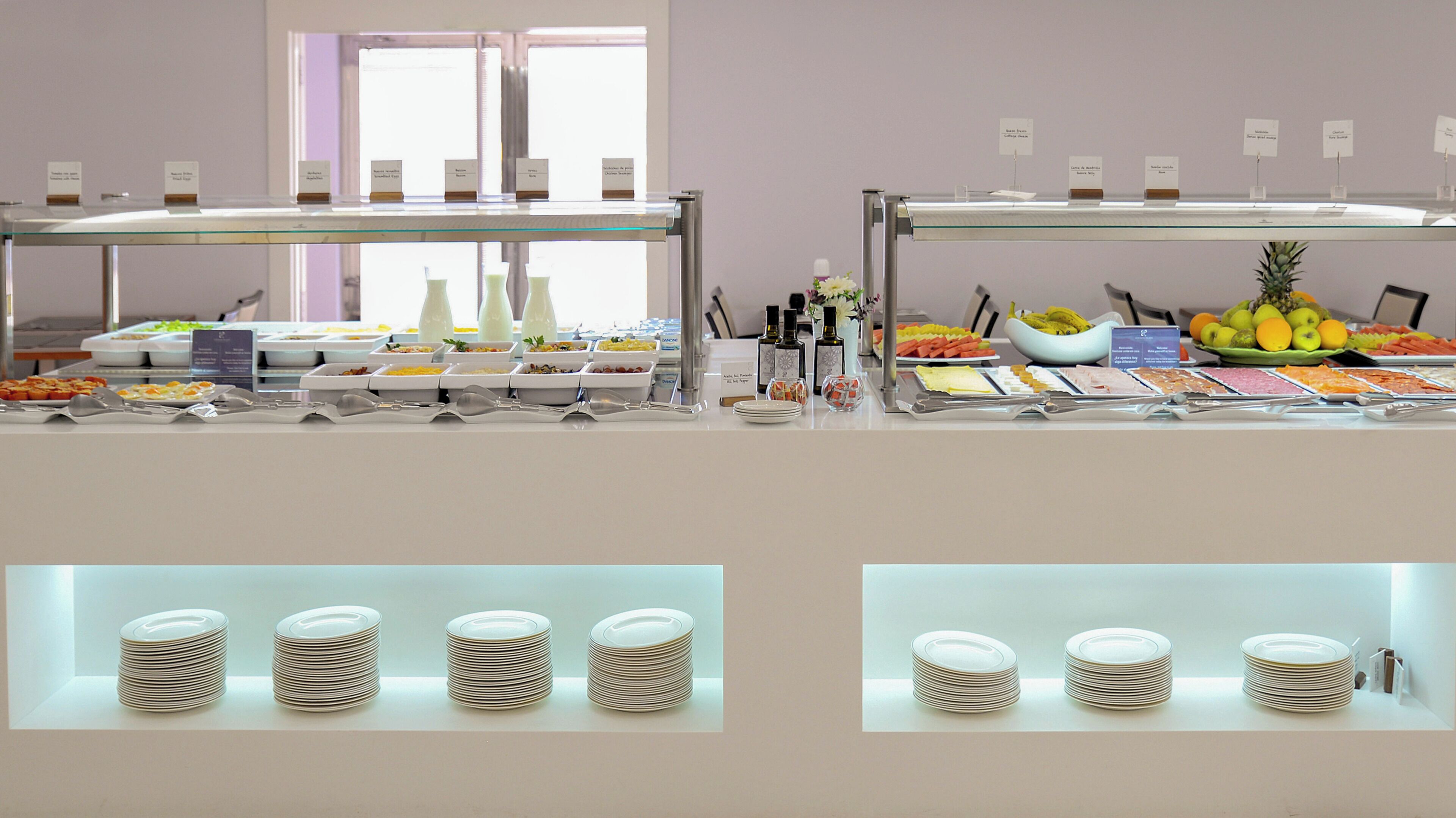Disposição de buffet com diversos alimentos e acompanhamentos, organizados em vitrines de vidro.