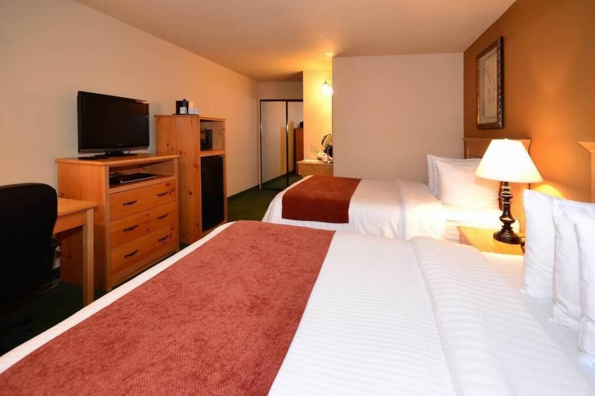 Quarto de hotel com duas camas, televisão, escrivaninha e guarda-roupa.