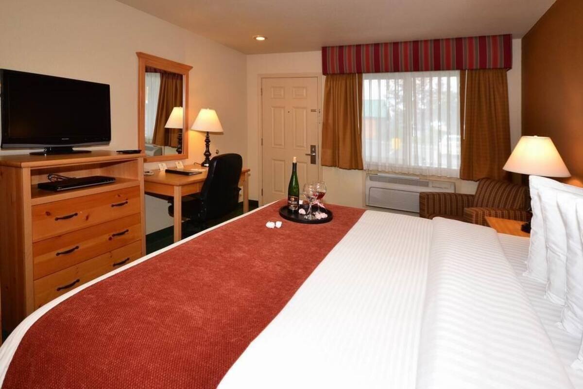 Quarto de hotel com uma cama, uma mesa de trabalho com um computador, uma televisão e uma janela com cortinas.