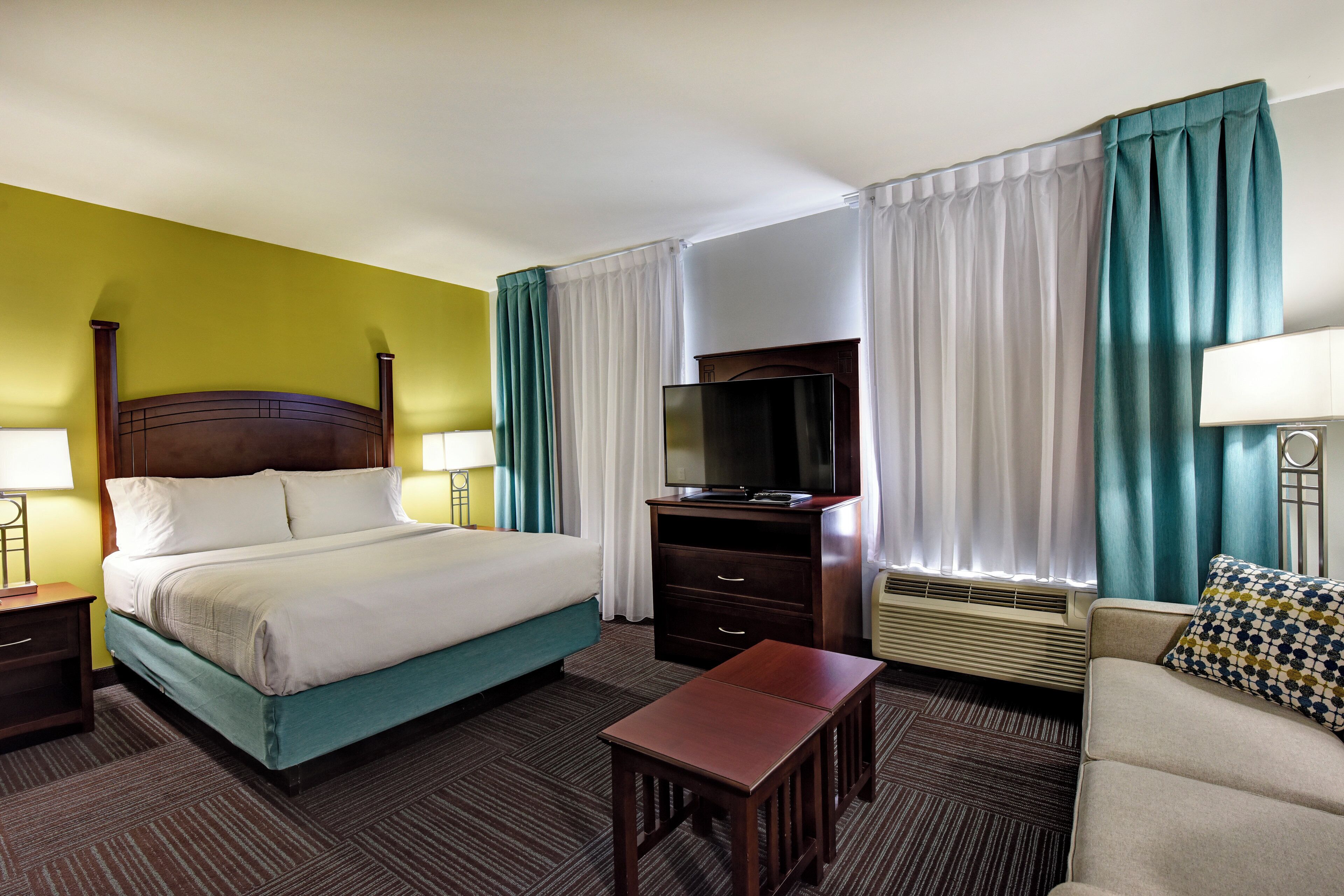 Quarto de hotel com cama, escrivaninha, televisão e sofá.
