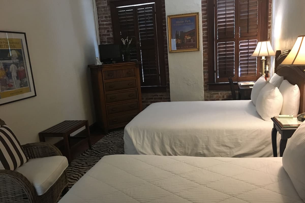 Quarto de hotel com duas camas, cômoda de madeira, tapete com padrão de zebra, cadeira de vime e quadro na parede.