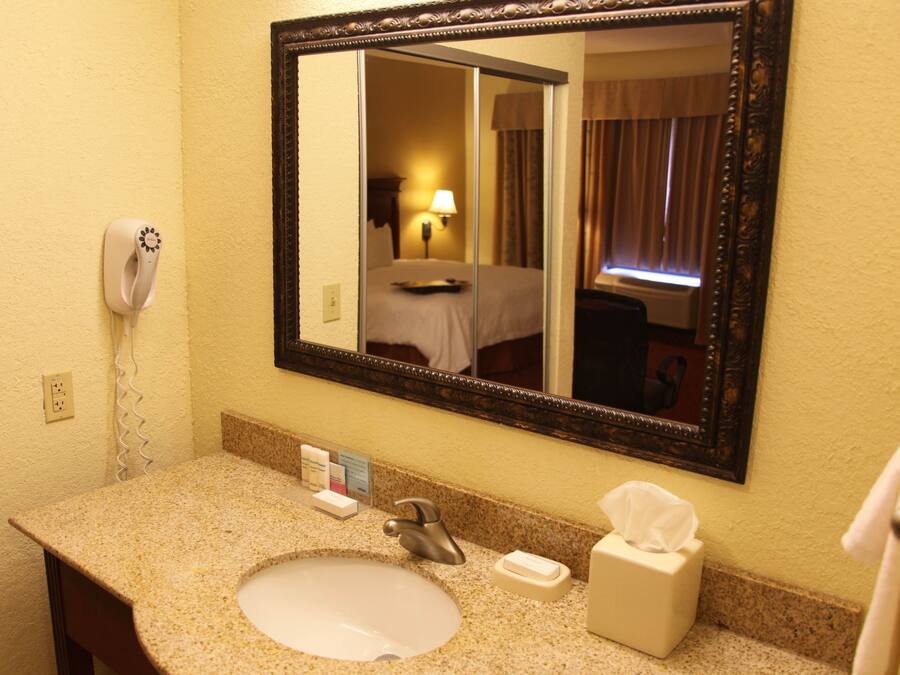 Casa de banho de hotel com lavatório, espelho, toalheiro e secador de mãos.