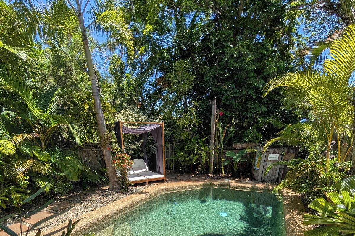 Piscina límpida rodeada por vegetação exuberante e um pergolado de madeira.