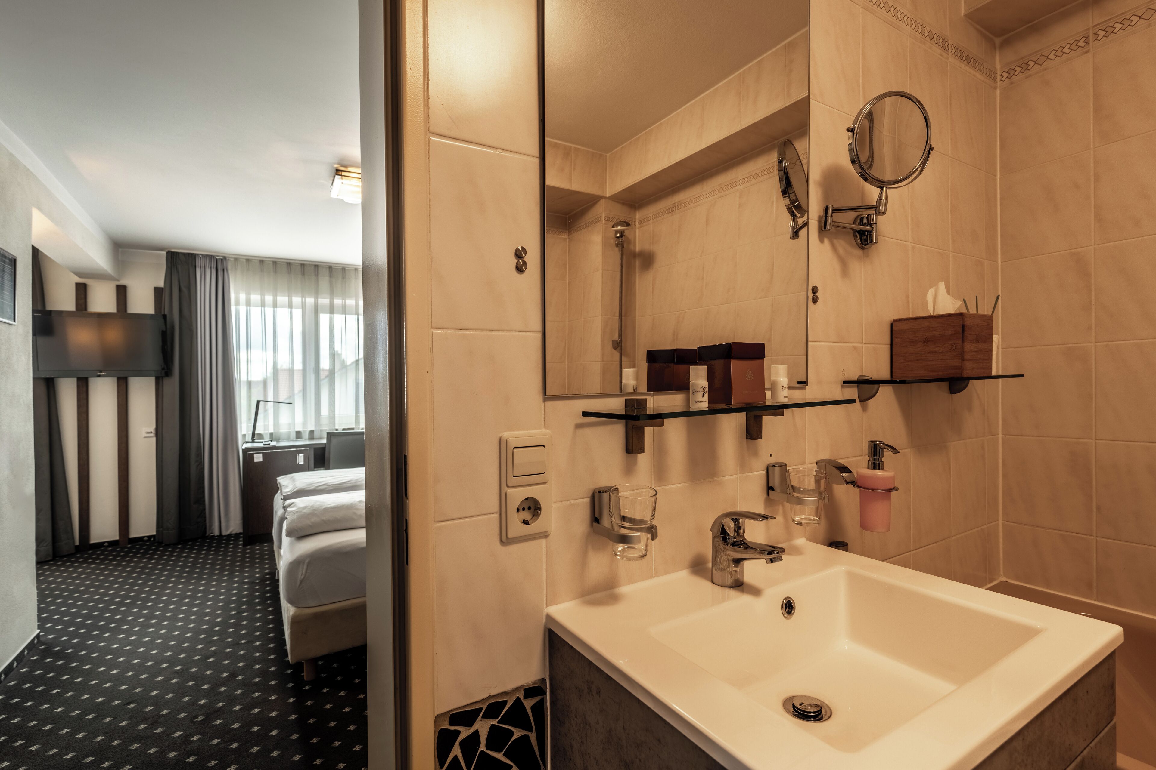 Quarto de hotel com uma cama grande, uma televisão, um banheiro com pia, espelho e prateleiras.